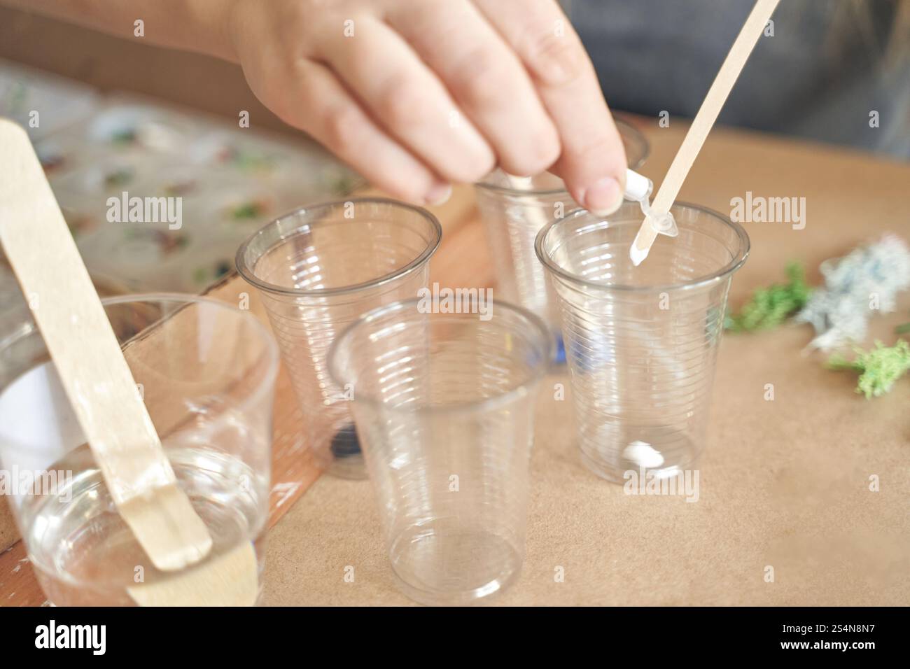 Hands preparing resin mixture with wooden sticks in clear plastic cups ...