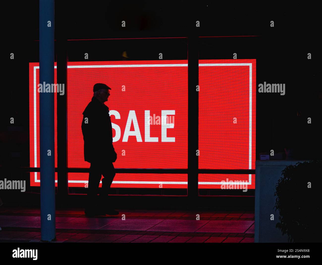 Silhouette of male shopper walking in front of an electronic sale sign ...