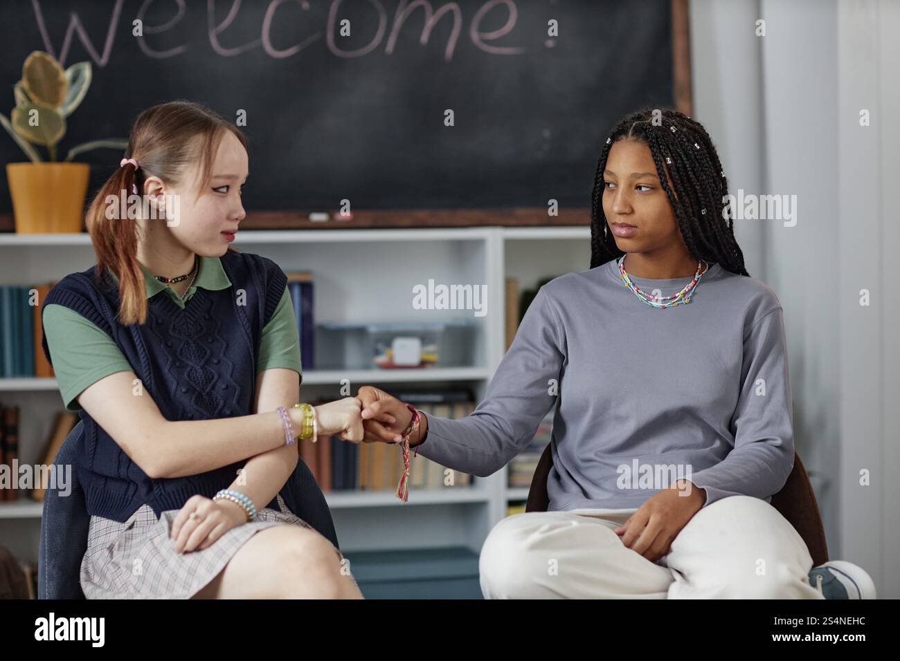 Side view portrait of two teenage girls doing fist bump while sitting ...