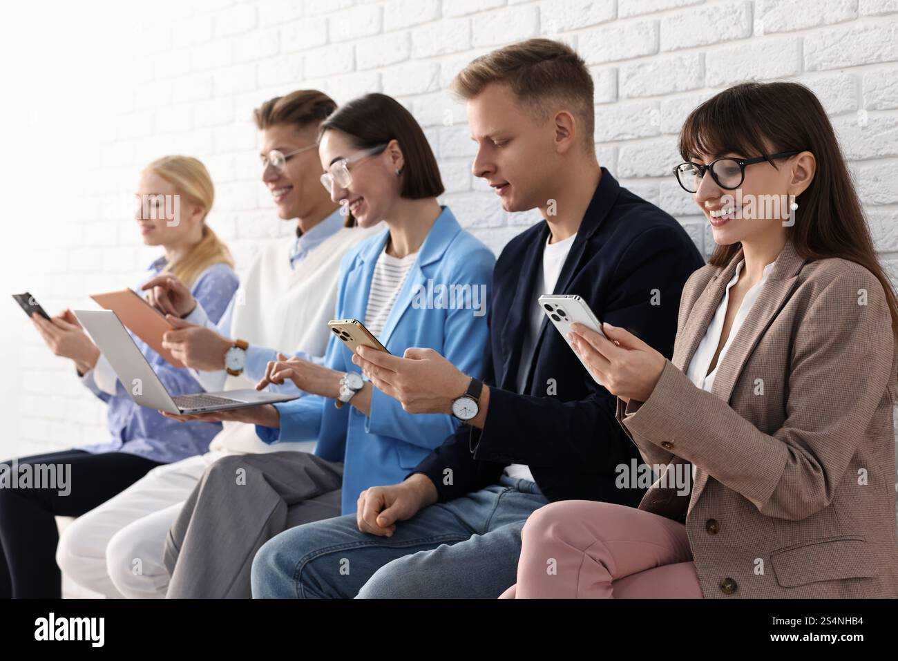 Group of people using different gadgets near white brick wall indoors ...