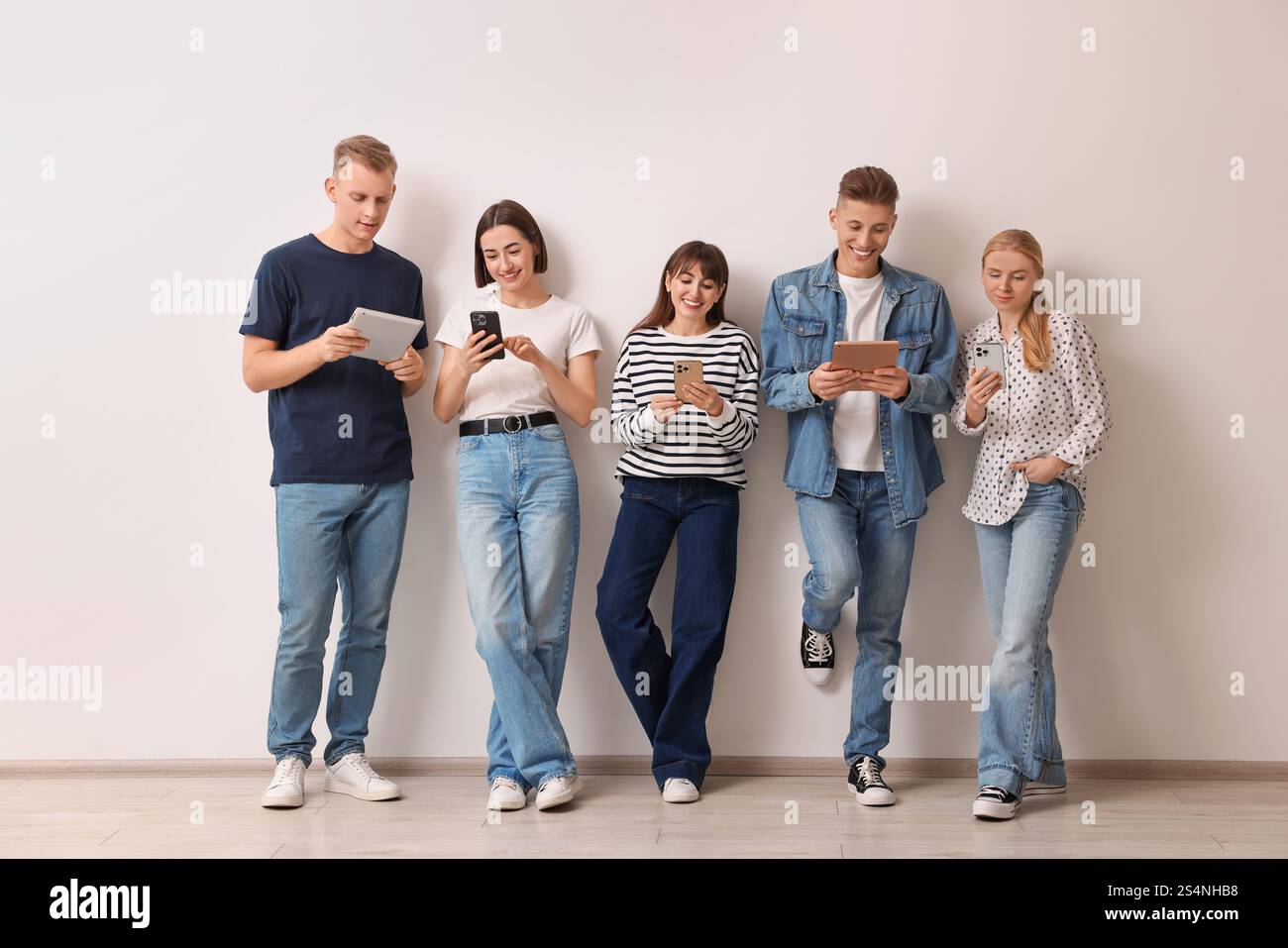 Group of people using different gadgets near white wall indoors. Modern ...