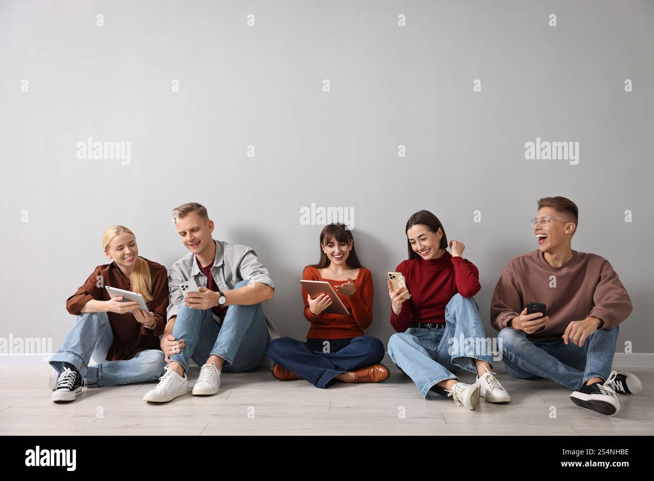 Group of people using different gadgets near light grey wall indoors ...