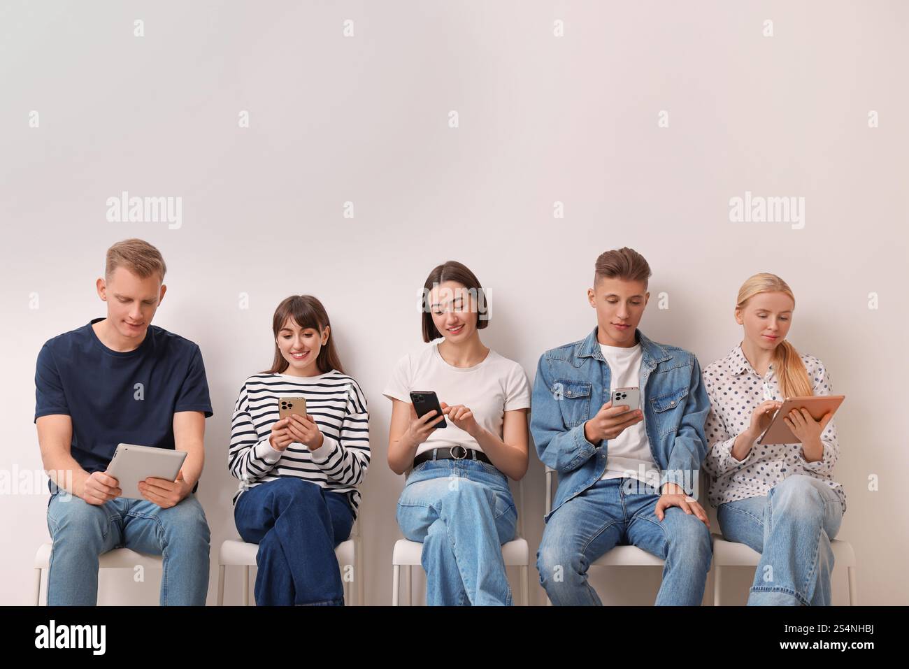 Group of people using different gadgets on chairs near white wall ...