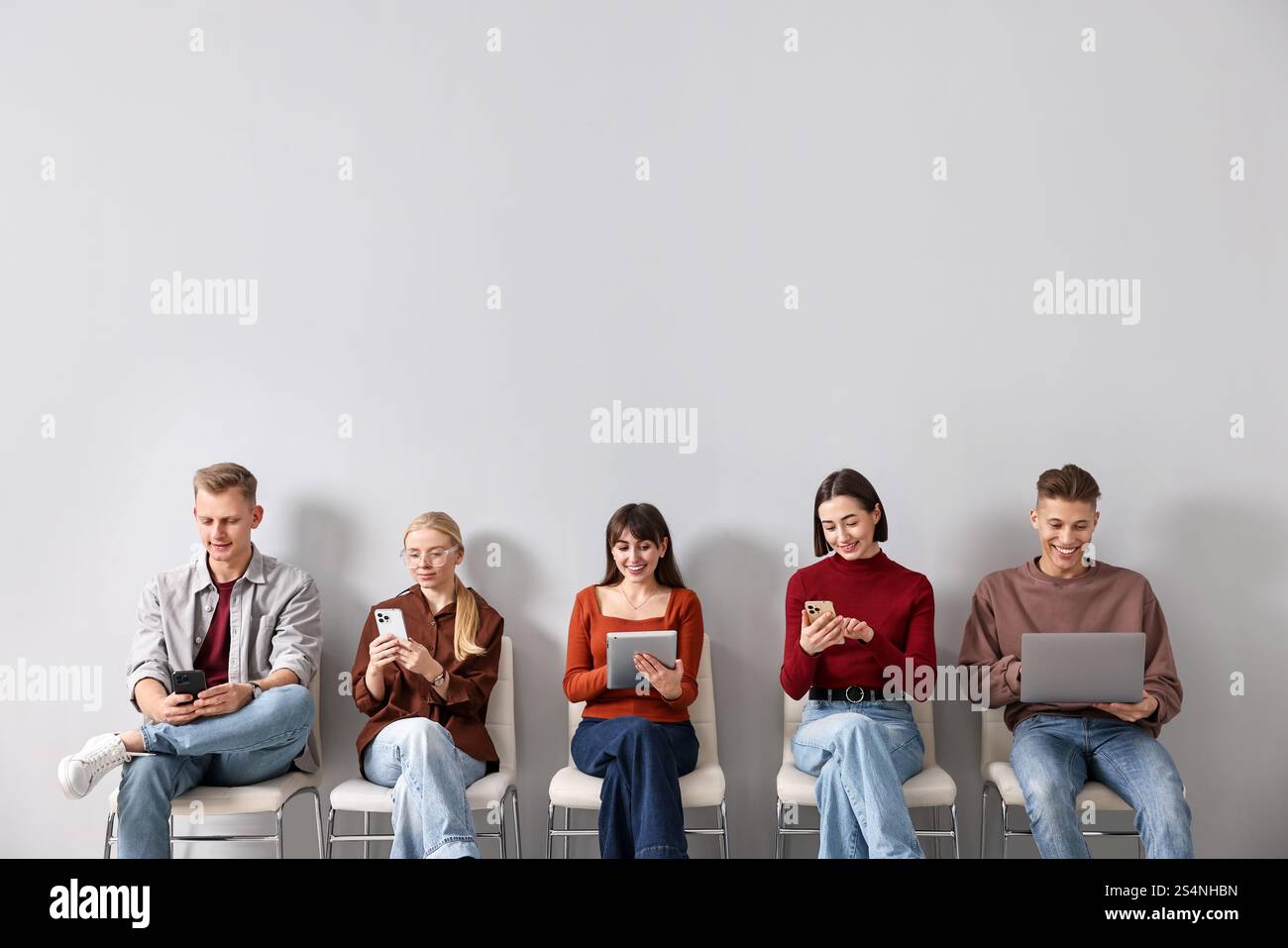 Group of people using different gadgets on chairs near light grey wall ...