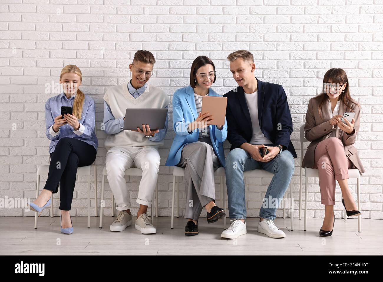 Group of people using different gadgets on chairs near white brick wall ...