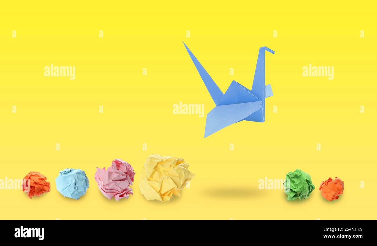 Blue origami crane and crumpled paper balls on yellow gradient ...