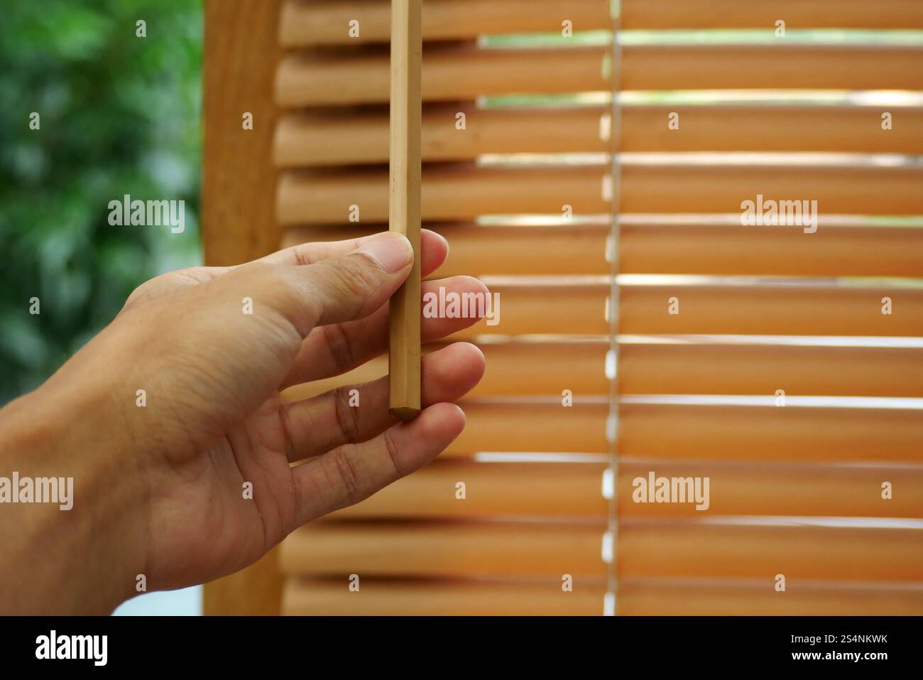 A man's hand turns a control lever that closes the wooden window slats ...