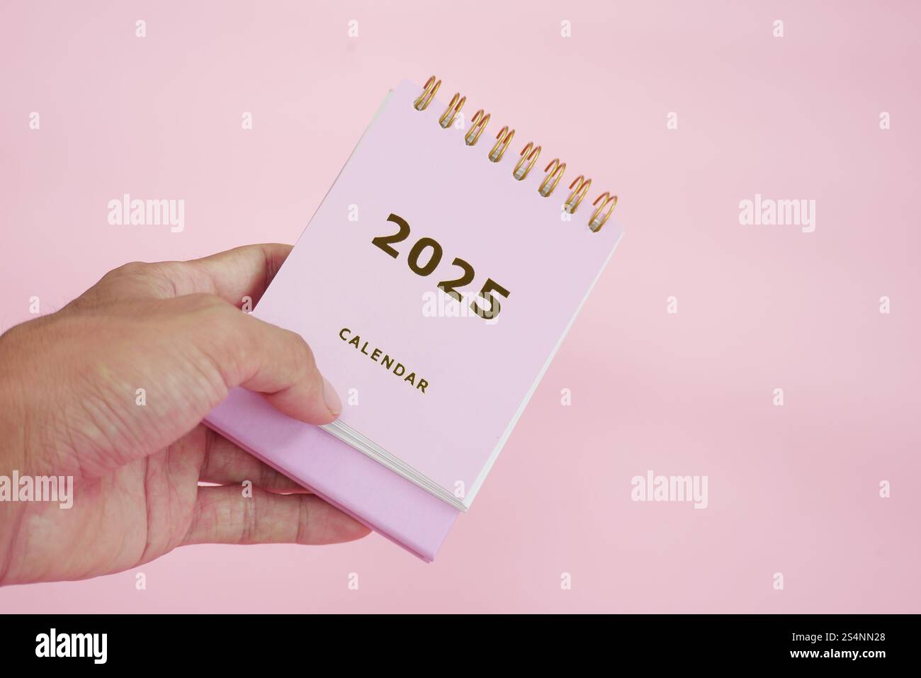 A hand holding a pink desk calendar 2025 in pink background Stock Photo ...