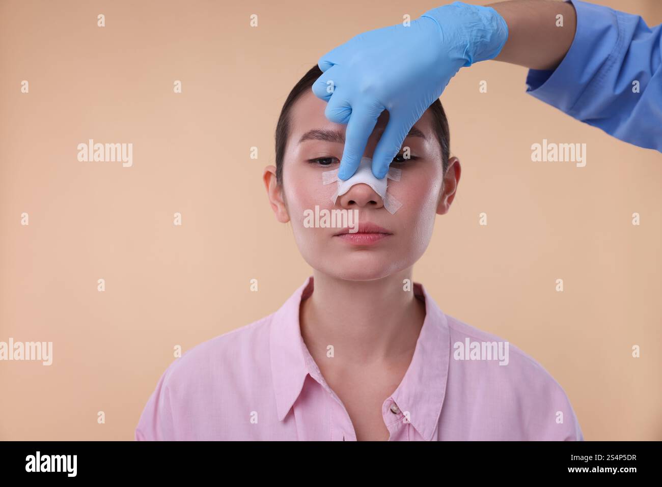 Doctor checking patient's nose after plastic surgery operation on beige ...