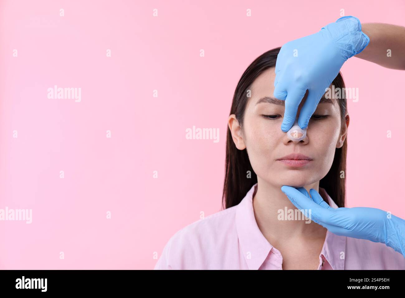 Doctor checking patient's nose after plastic surgery operation on pink ...