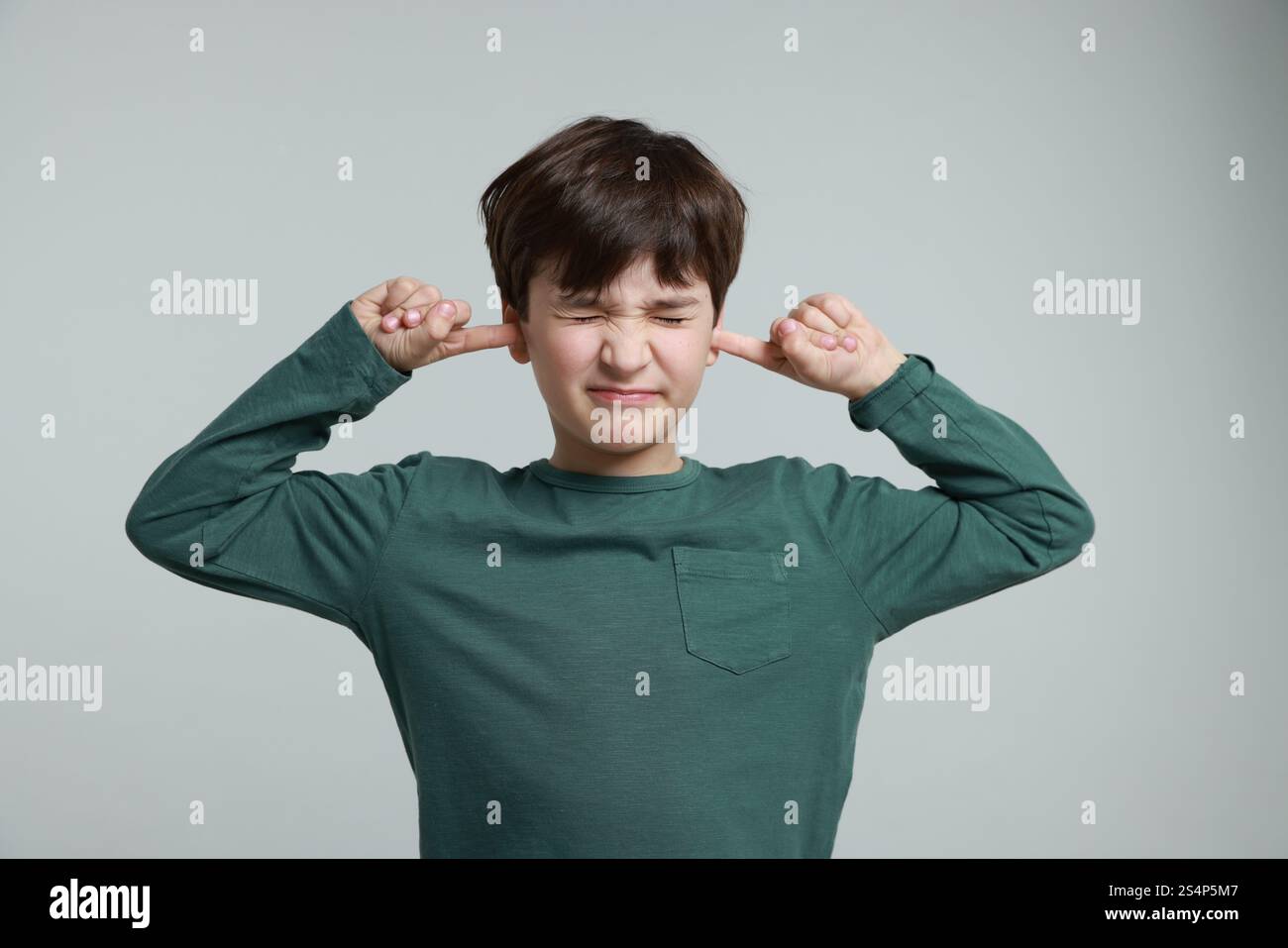 Annoyed boy covering his ears due to loud sound on grey background ...
