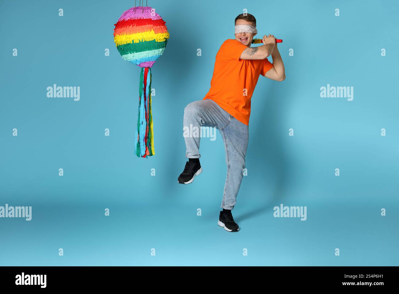 Man with tied eyes breaking pinata on light blue background Stock Photo ...