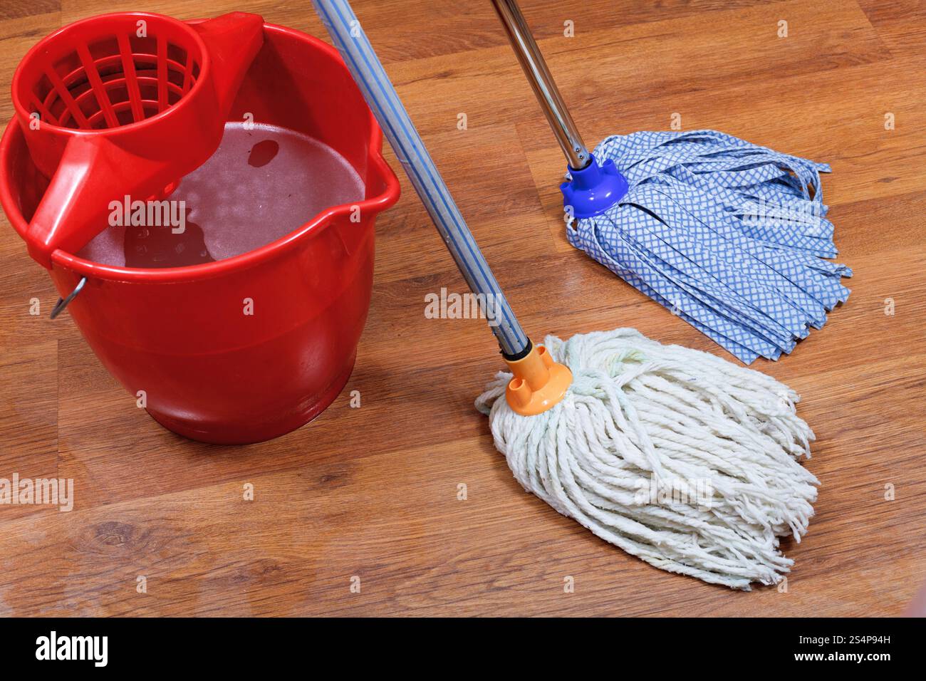 cleaning of wet floors by two mops and red bucket with washing water ...