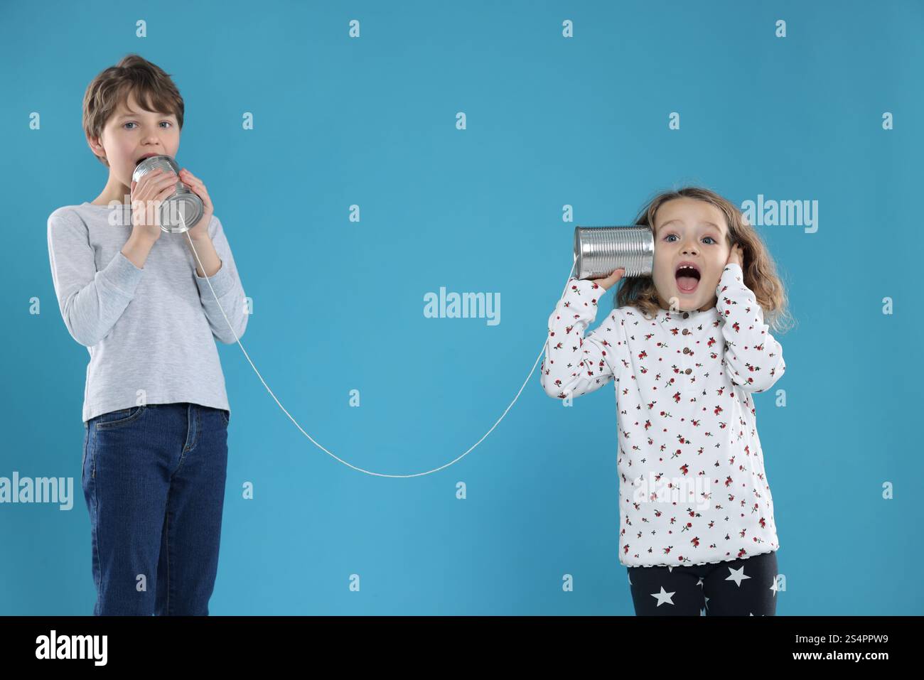 Boy and girl talking on tin can telephone against blue background Stock ...