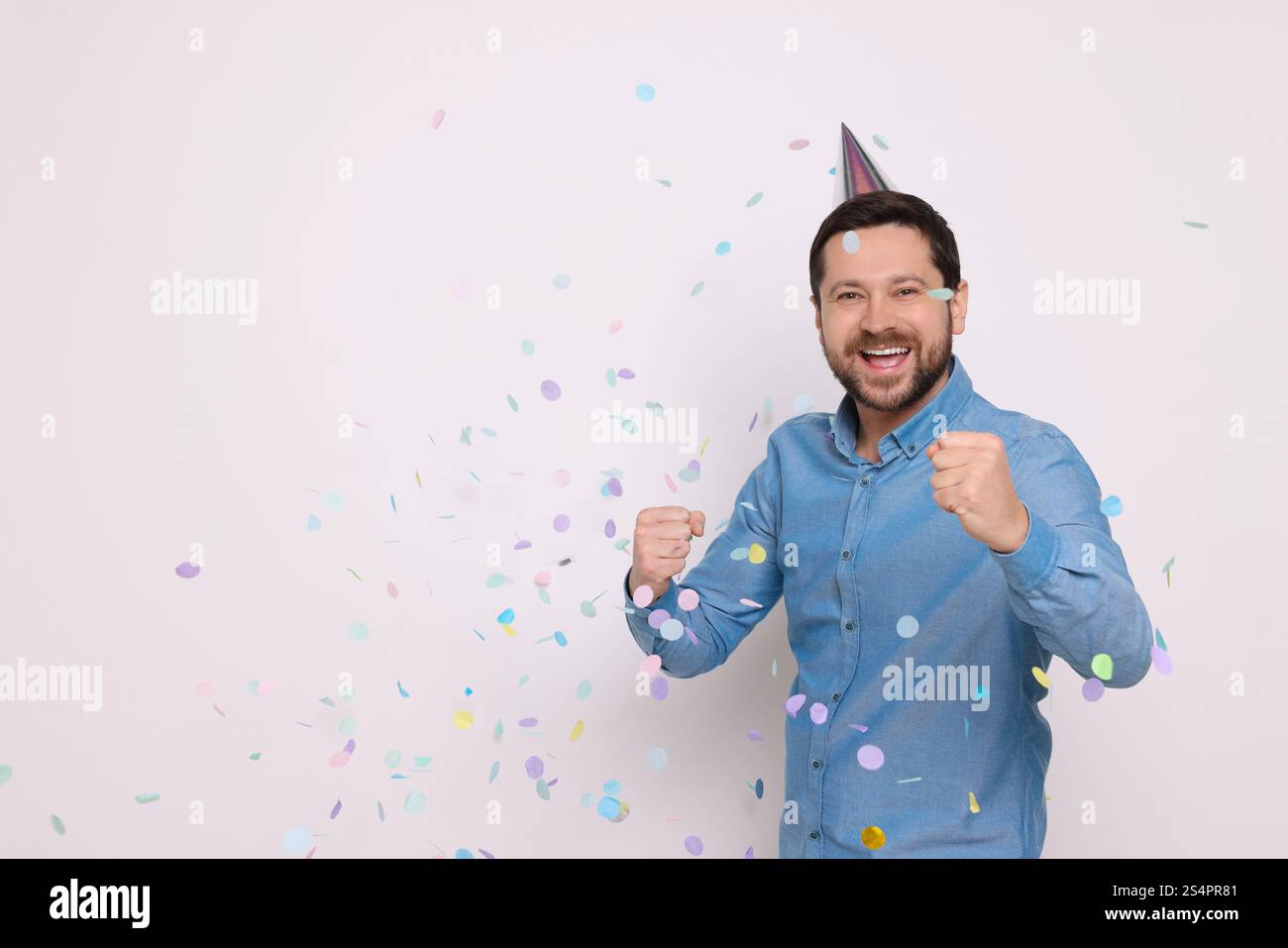 Happy man in conical paper hat and falling confetti on white background ...