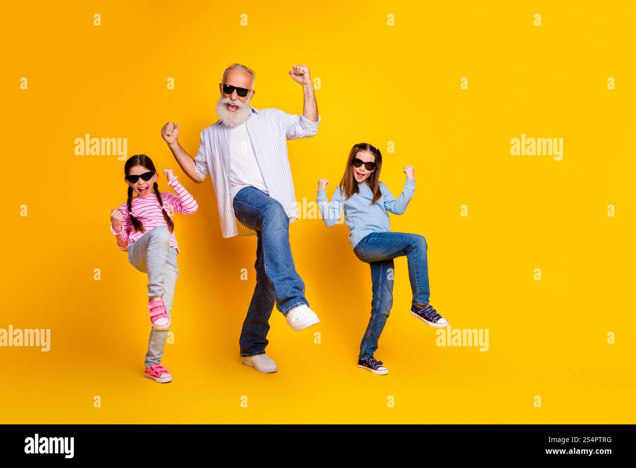 Joyful grandfather dancing with his granddaughters on a vibrant yellow ...