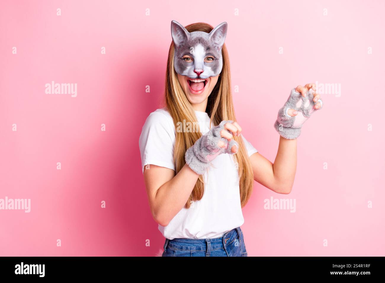 Playful girl with cat costume posing on a pink background, expressing ...