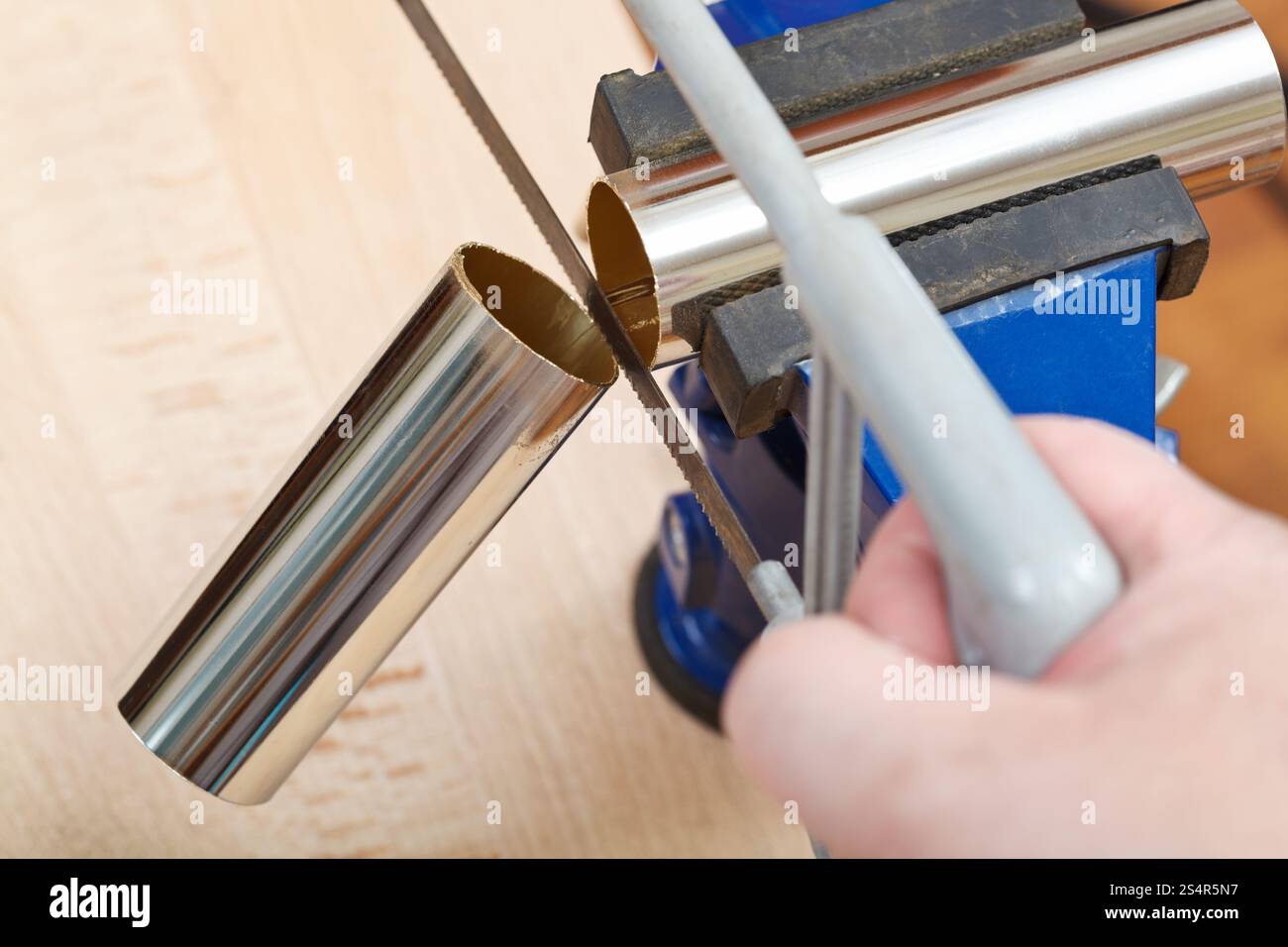 mechanic saws chrome-plated drain pipe gripped in vice by hacksaw close ...