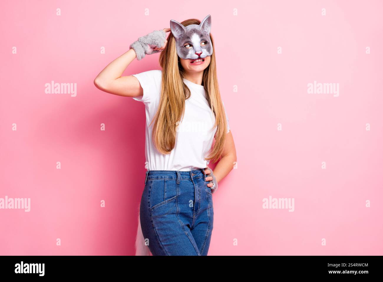 Young woman wearing a cat mask posing playfully with a pink background ...
