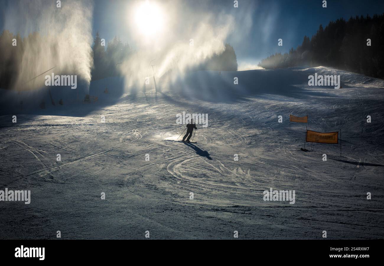 Professional skier going down the slope under working snow cannons ...
