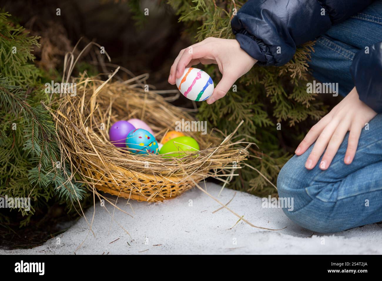 Closeup photo of little girl putting easter egg in nest at cold snowy ...