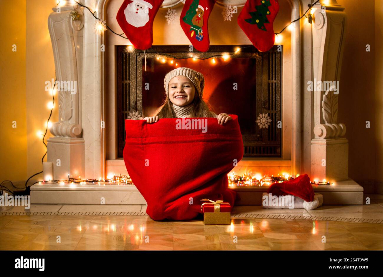Little girl sitting in big red sack at room decorated for Christmas ...
