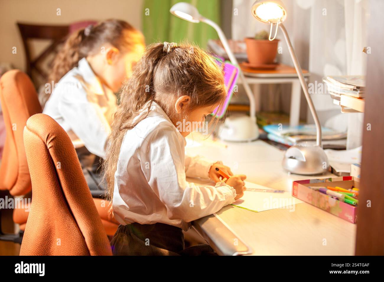 Two little girls drawing pictures behind desk Stock Photo - Alamy