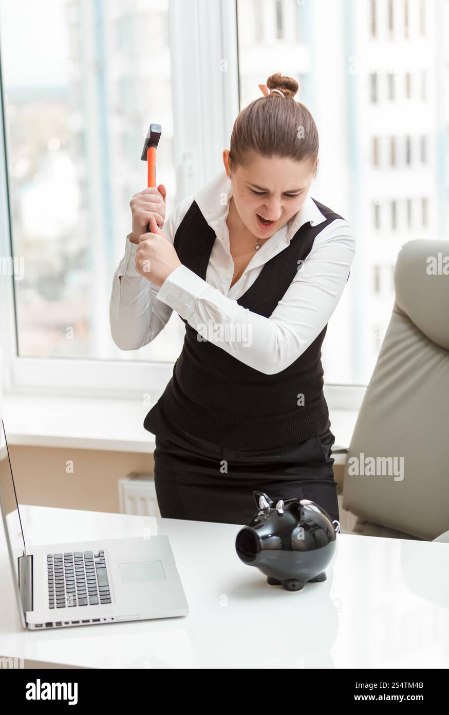 Portrait of angry woman at office hitting piggy bank with hammer Stock ...