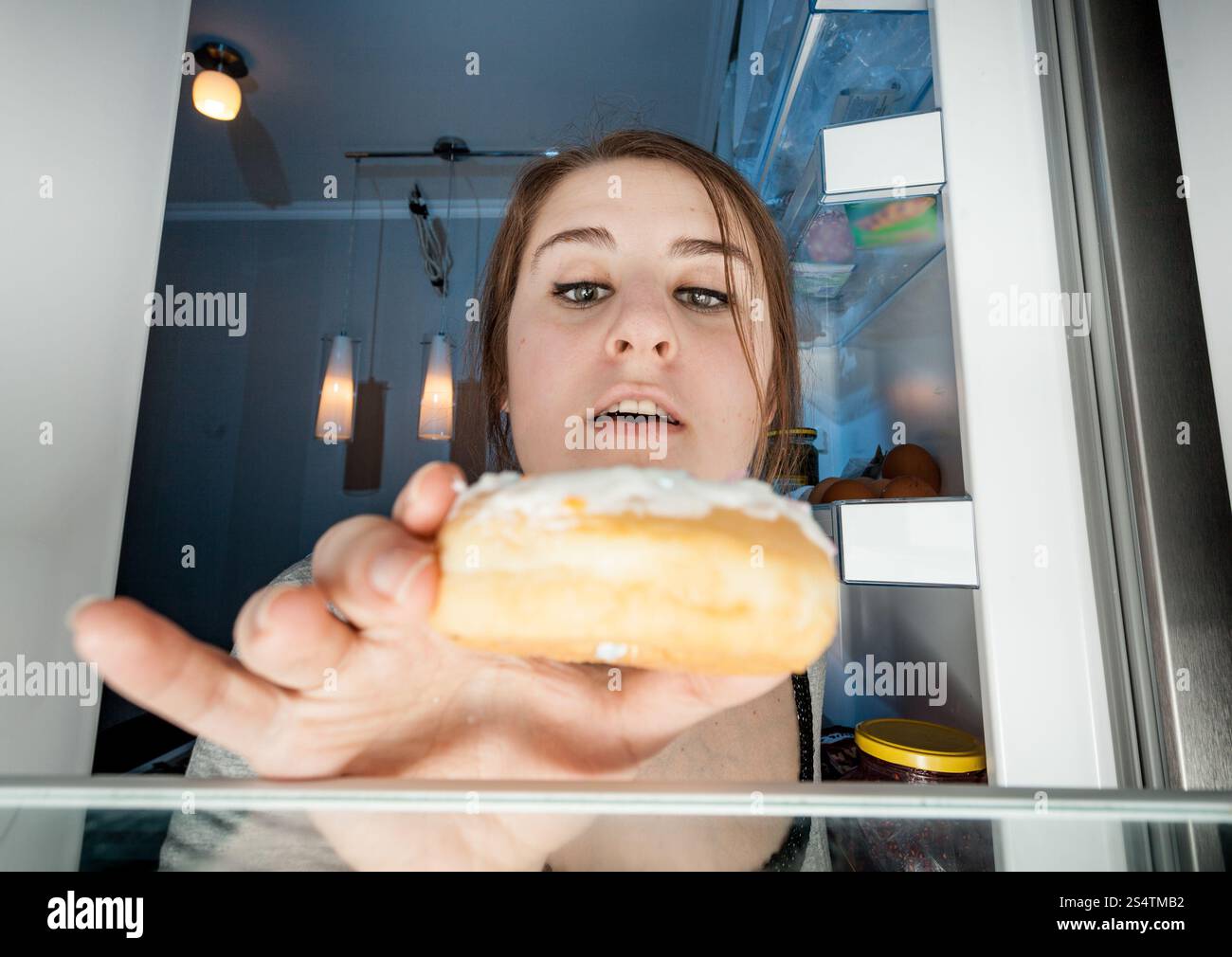Wide angle portrait of woman taking donut from fridge Stock Photo - Alamy