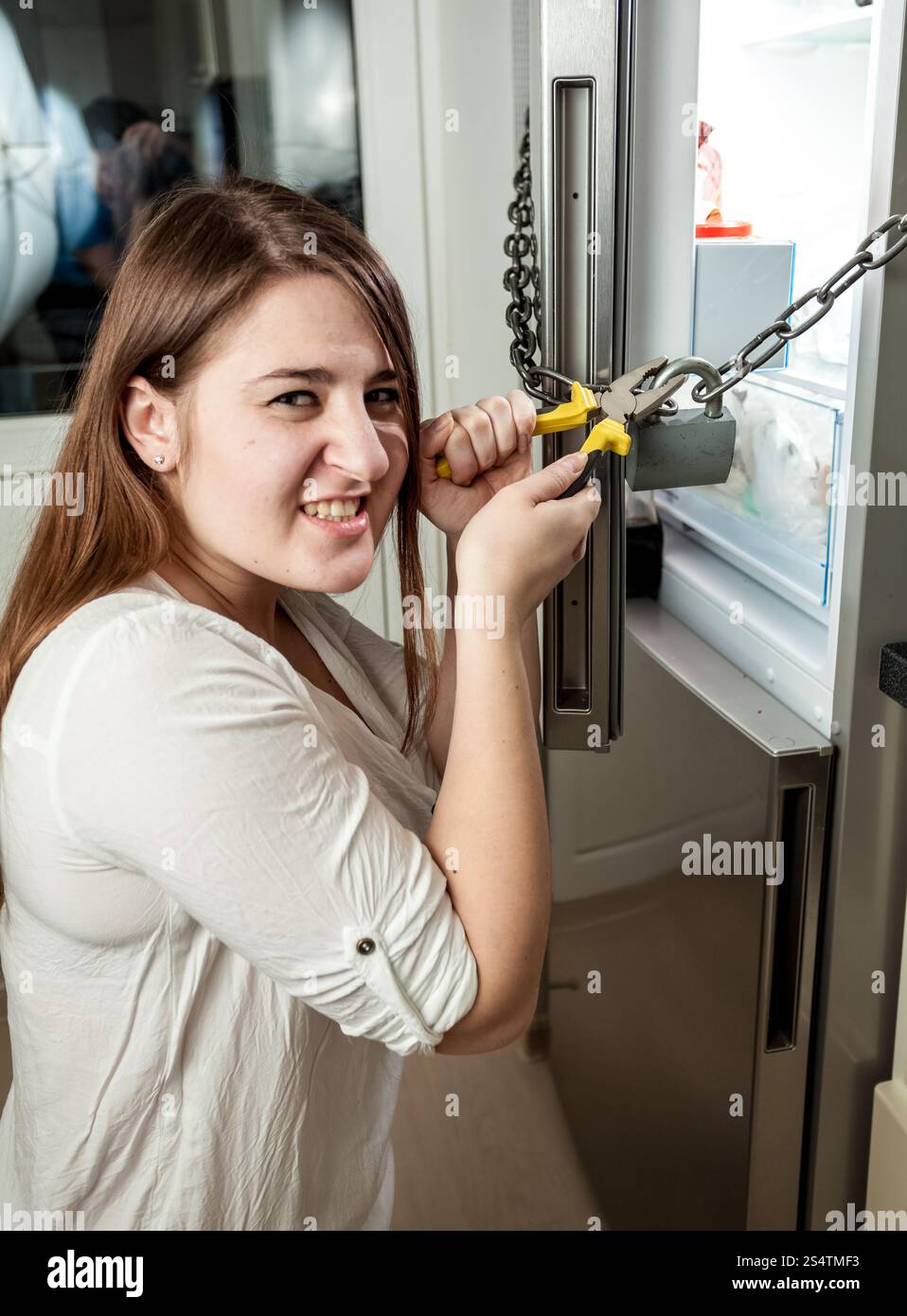 Portrait of angry woman cutting chain on refrigerator with cutters ...