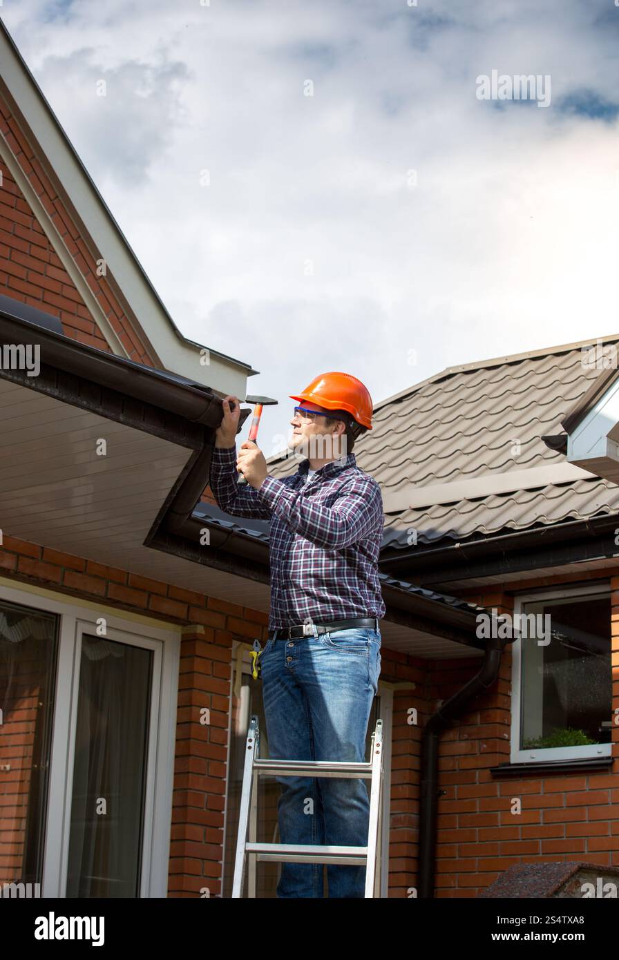 Professional carpenter standing on high ladder and repairing house roof ...