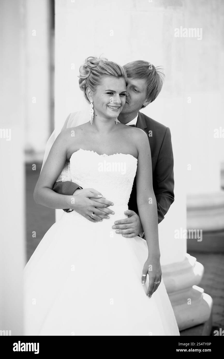 Black and white portrait of young groom hugging smiling bride from back ...