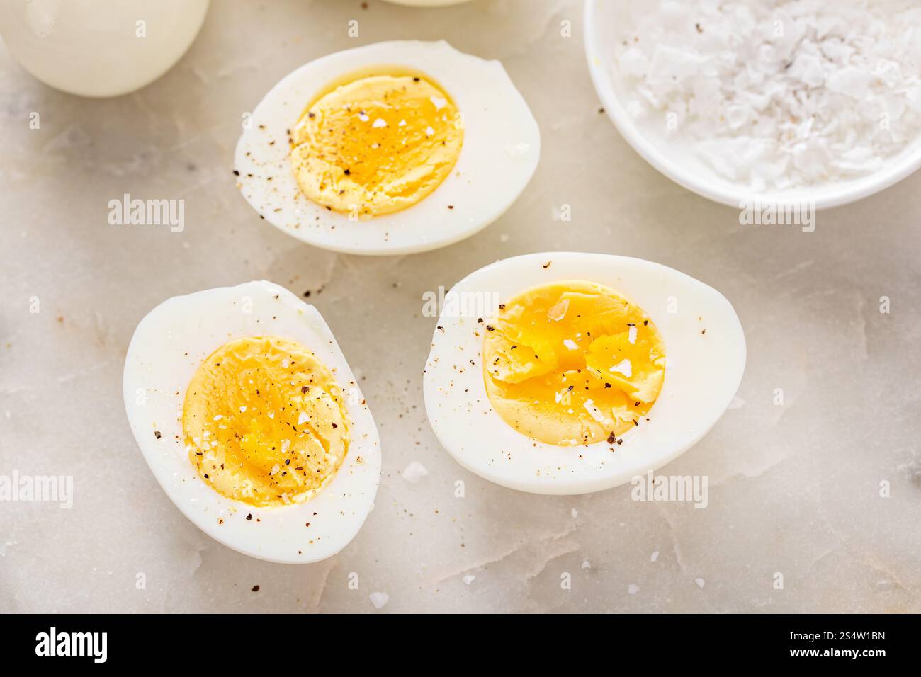 Soft boiled eggs cut in half with salt and black pepper Stock Photo - Alamy