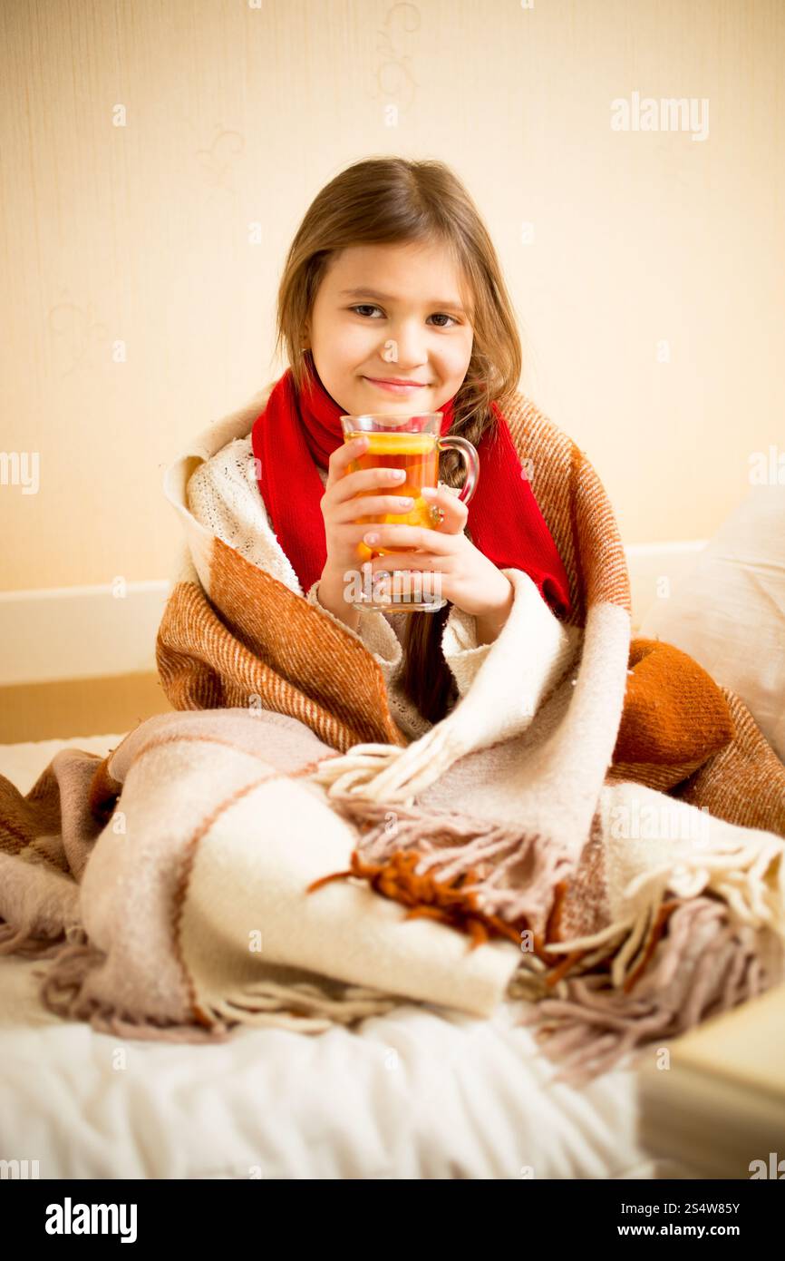 Portrait of cute girl covered in blanket drinking hot tea with lemon in ...