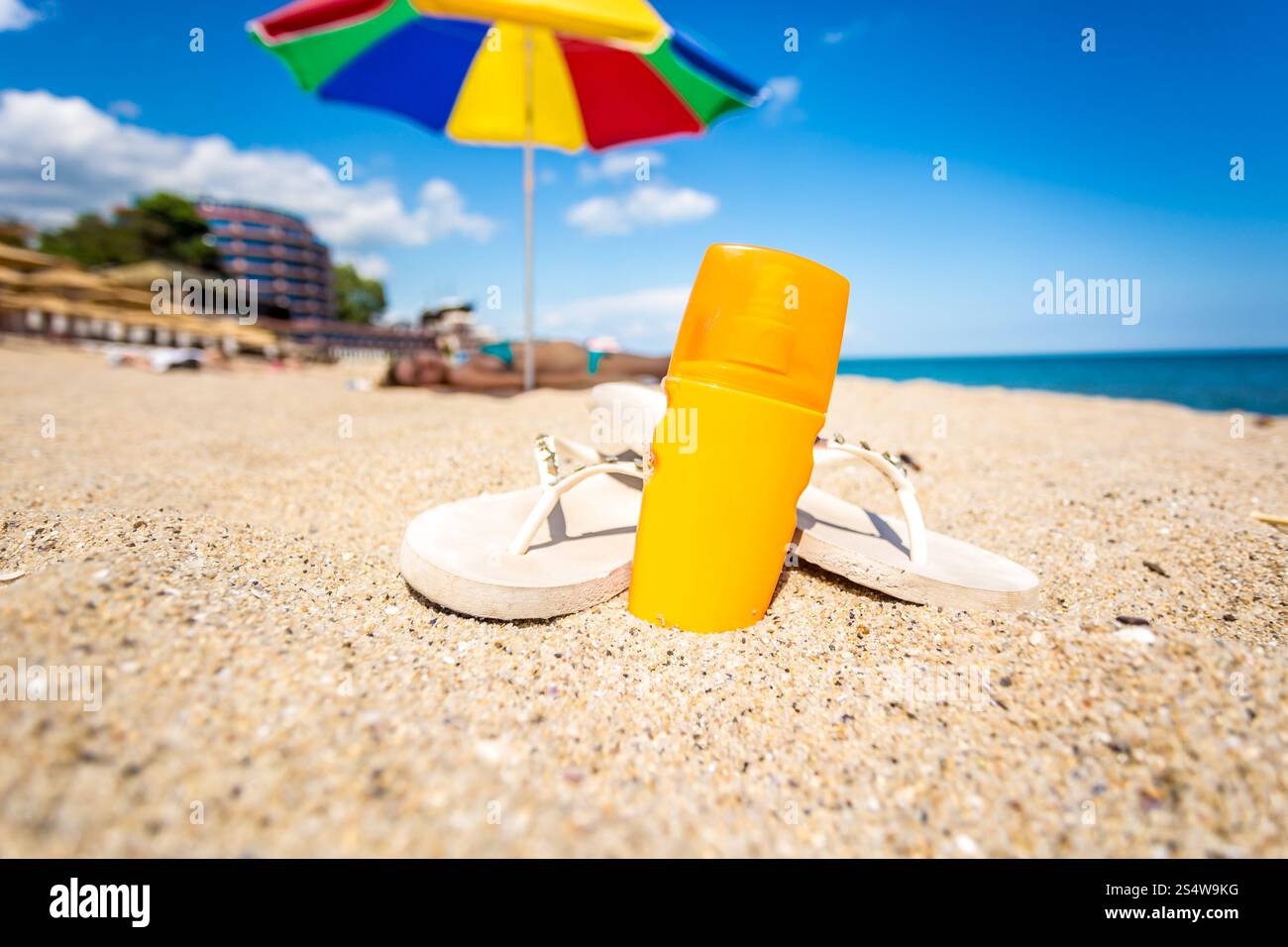 Closeup photo of yellow suntan lotion and flip flops lying on sandy ...