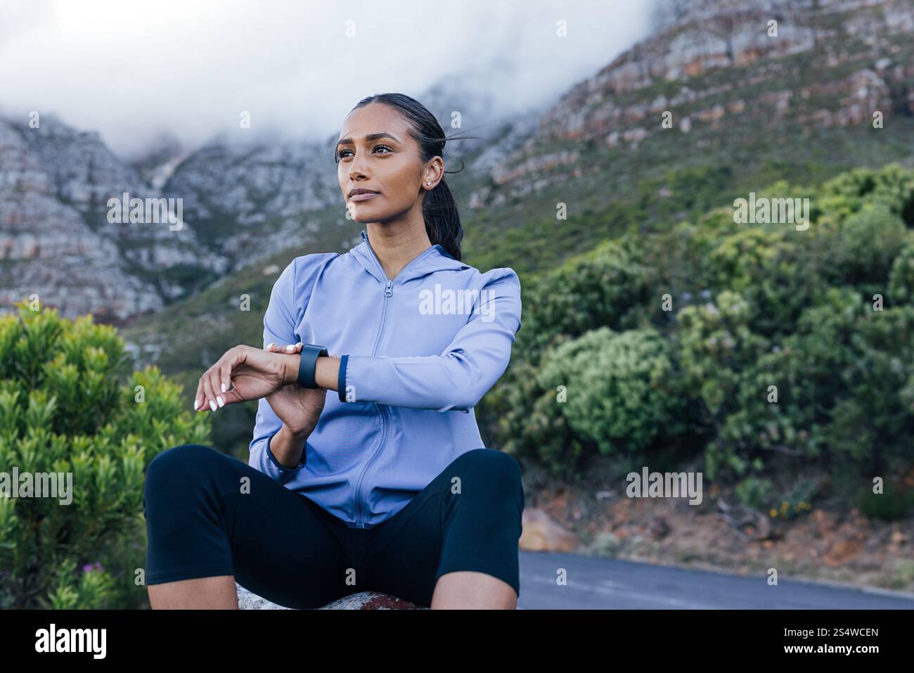 Slim woman in fitness attire sitting on the rock. Female using ...