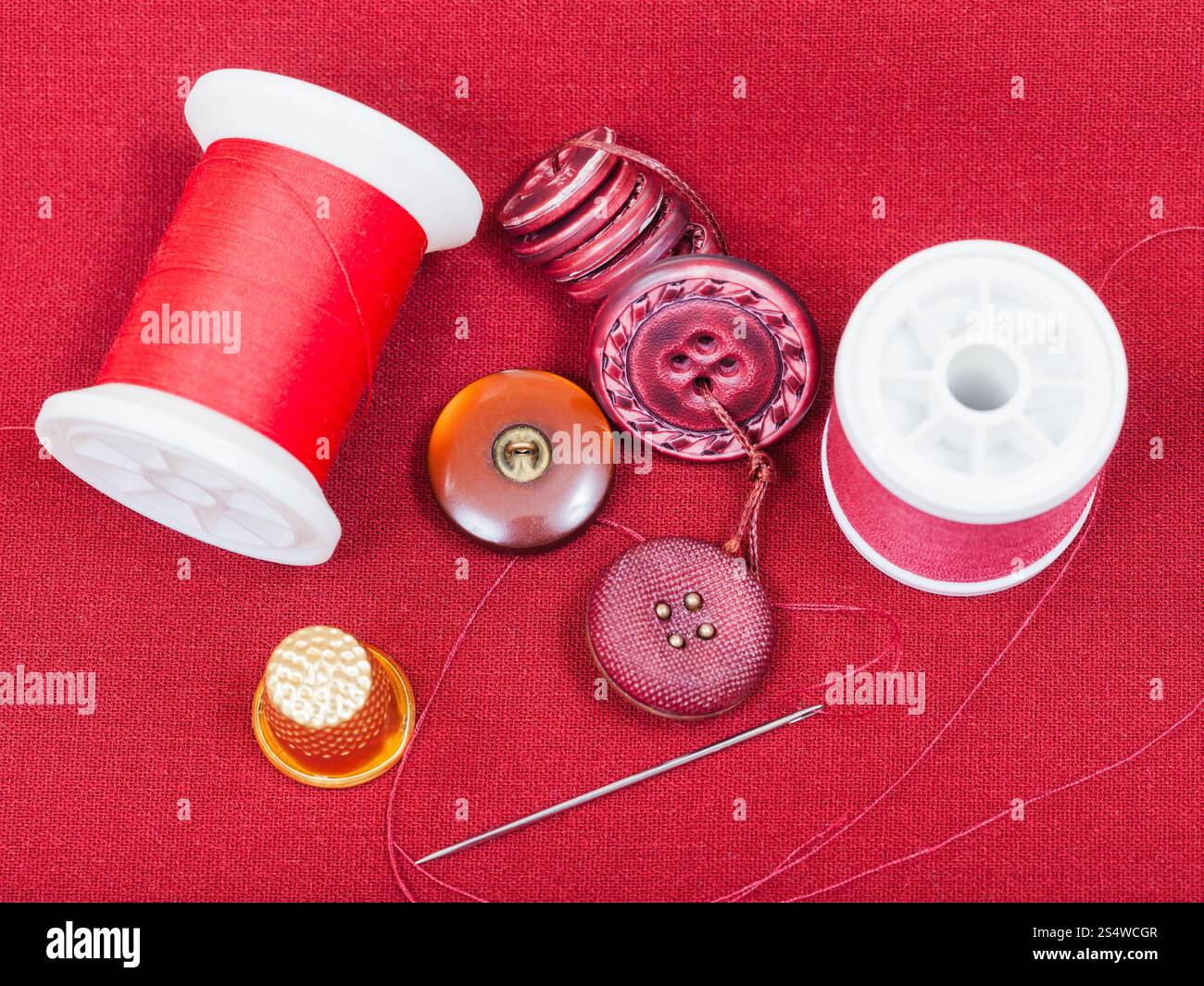 dressmaking still life - top view of bobbins with sewing thread, buttons, thimble, needle on red ...