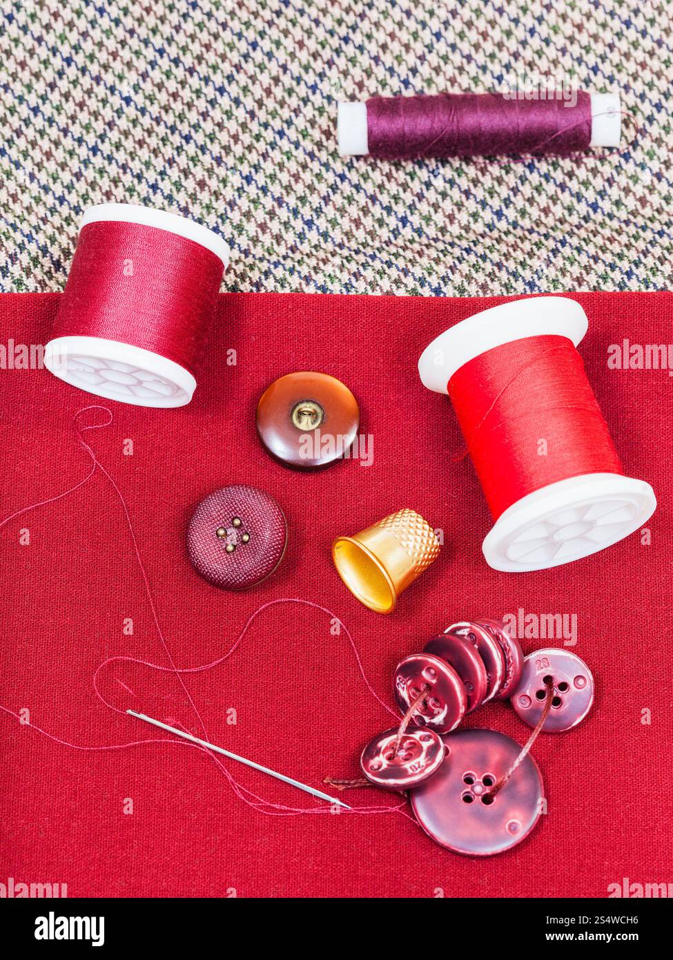 dressmaking still life - top view of bobbins with sewing thread, buttons, thimble, needle on red ...