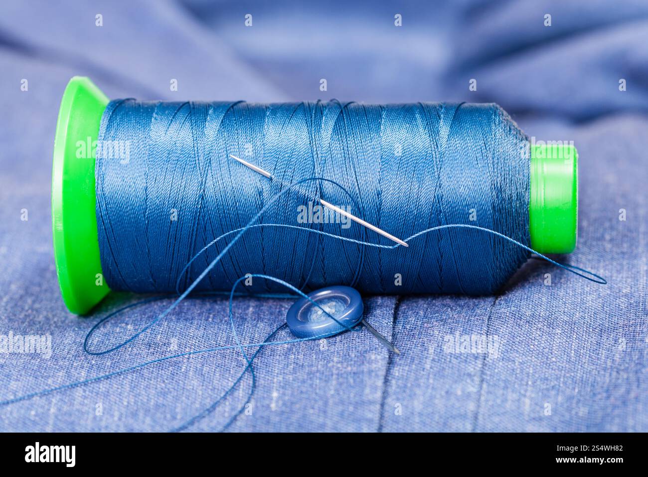 tailoring still life - thread bobbin with needle, button on blue silk ...