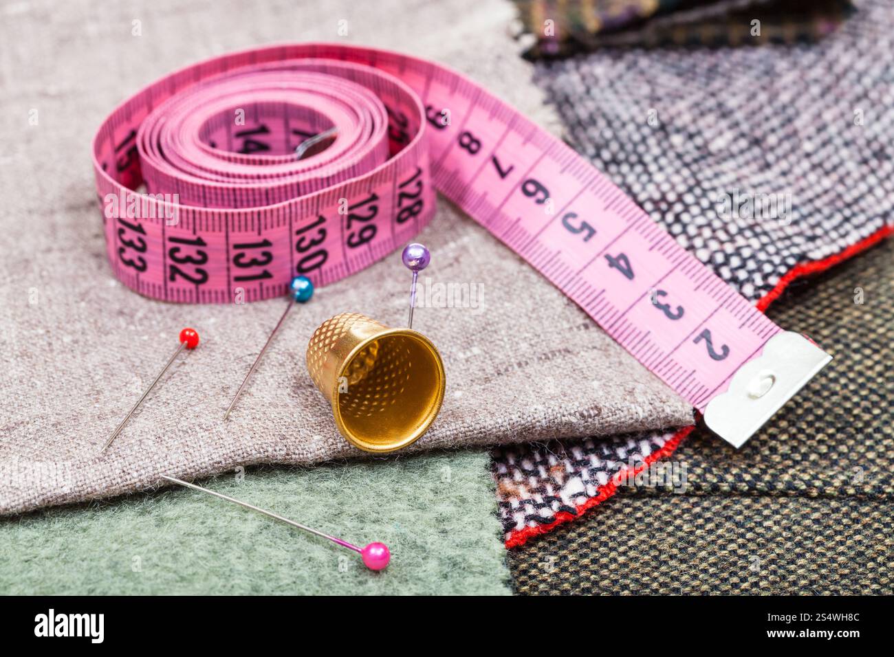 dressmaking still life - pink measure tape, pins, thimble on textile ...