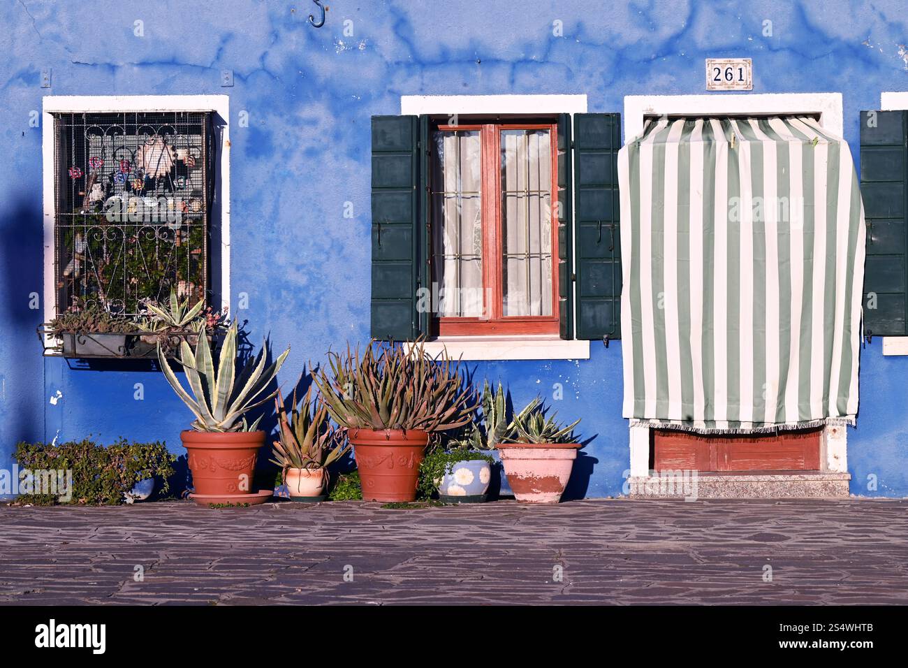 Colourful blue house façade with plants and a striped door covering on ...