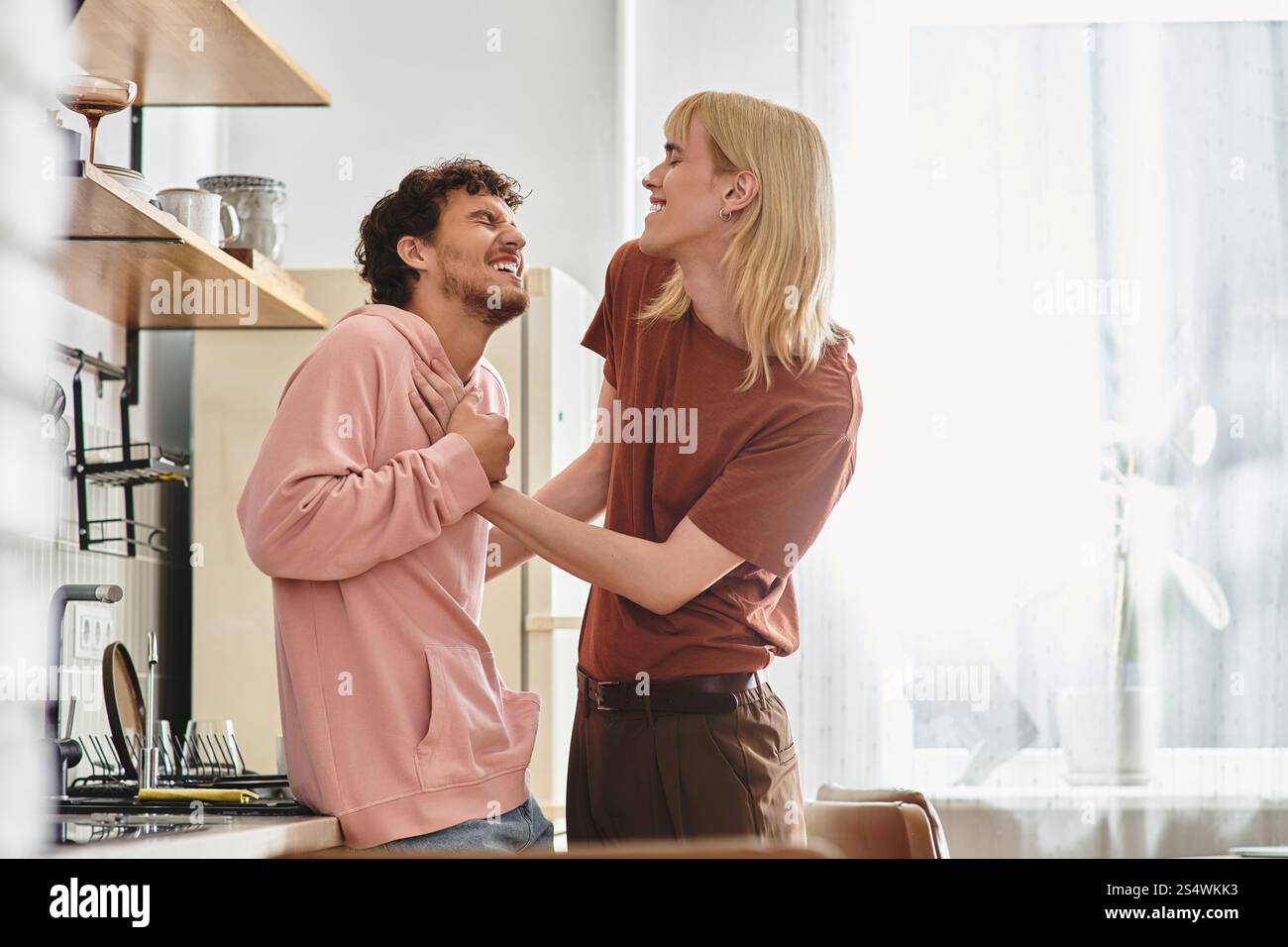 Two men embrace with laughter in a bright kitchen, cherishing their ...