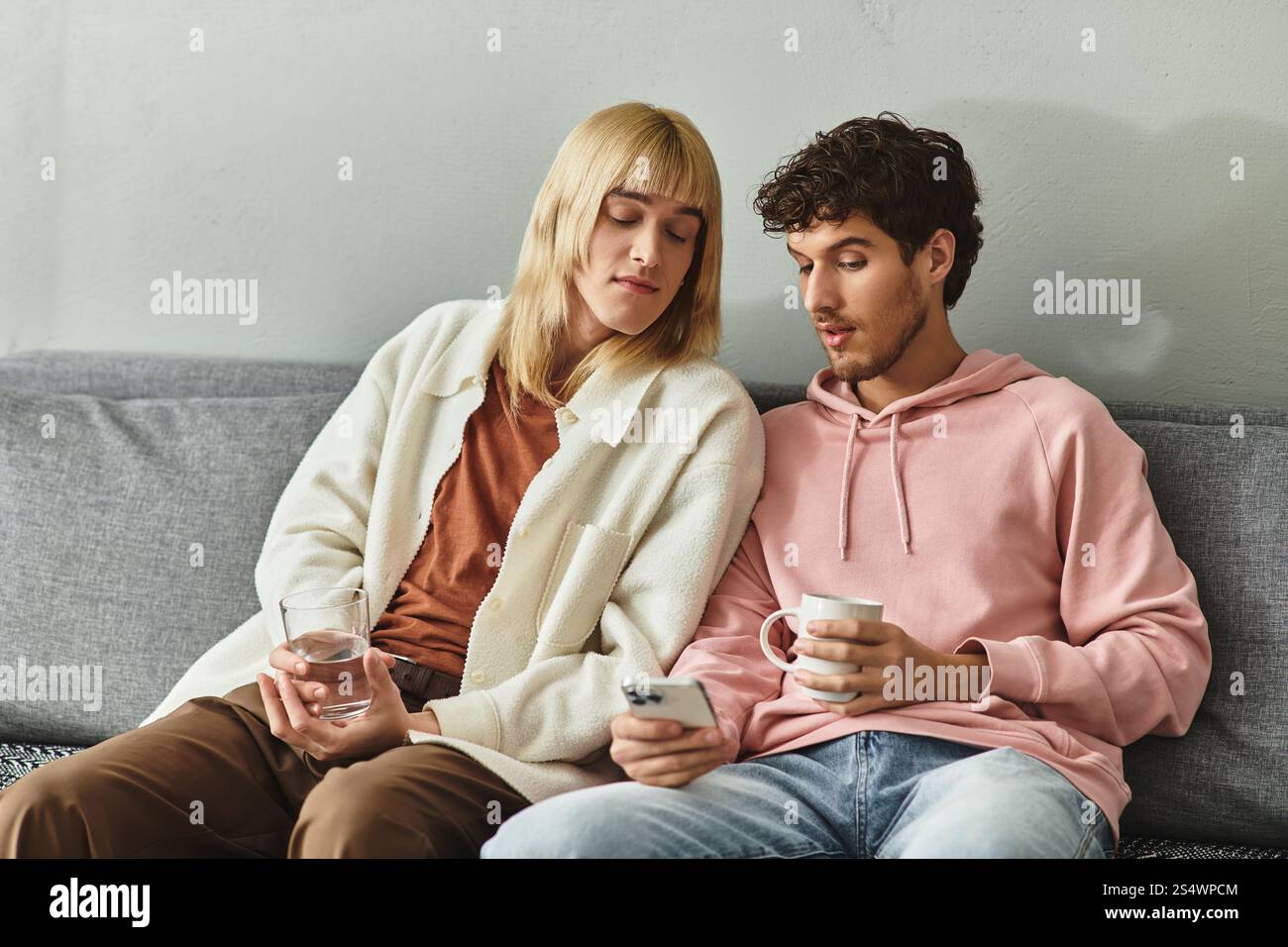 Two men share a tender moment on a couch, engaging with a mobile device ...