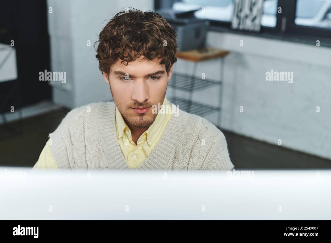 Curly-haired man in a sweater vest engages with his computer in a fresh ...