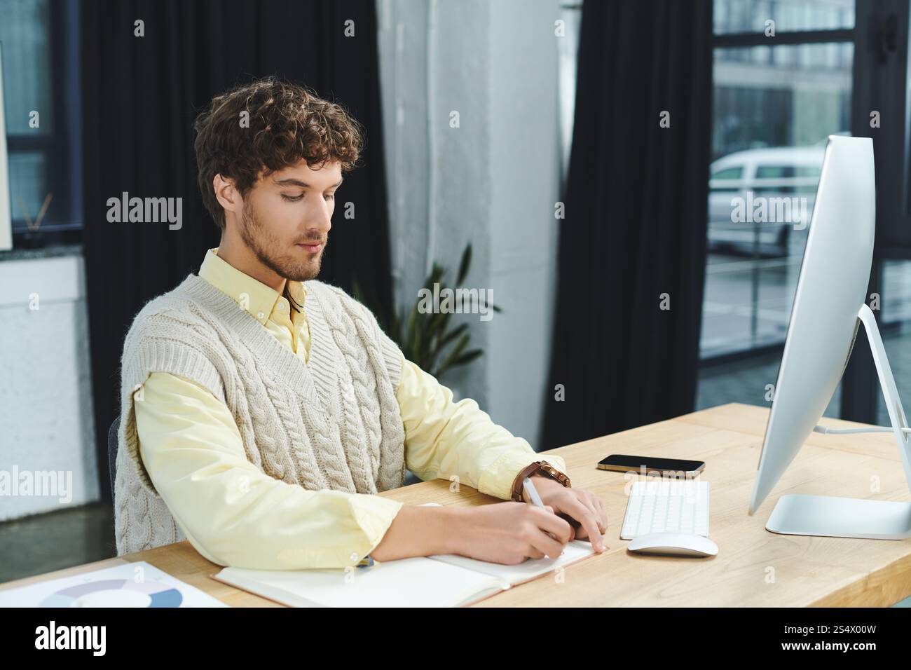 A young man with curly hair wears a sweater vest and diligently works ...