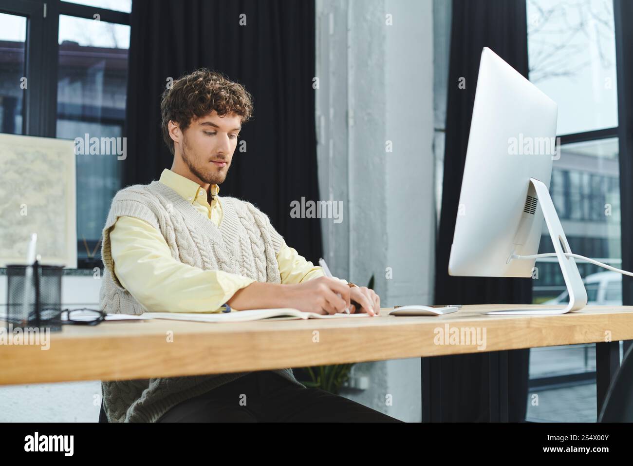 A young man with curly hair in a sweater vest diligently writes notes ...