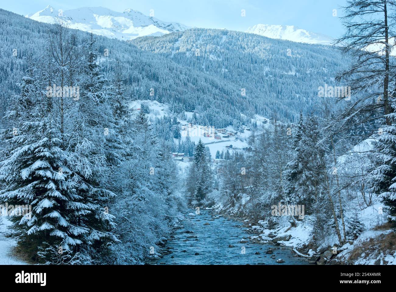 Winter mountain stream view and snowy forest and village on hill ...