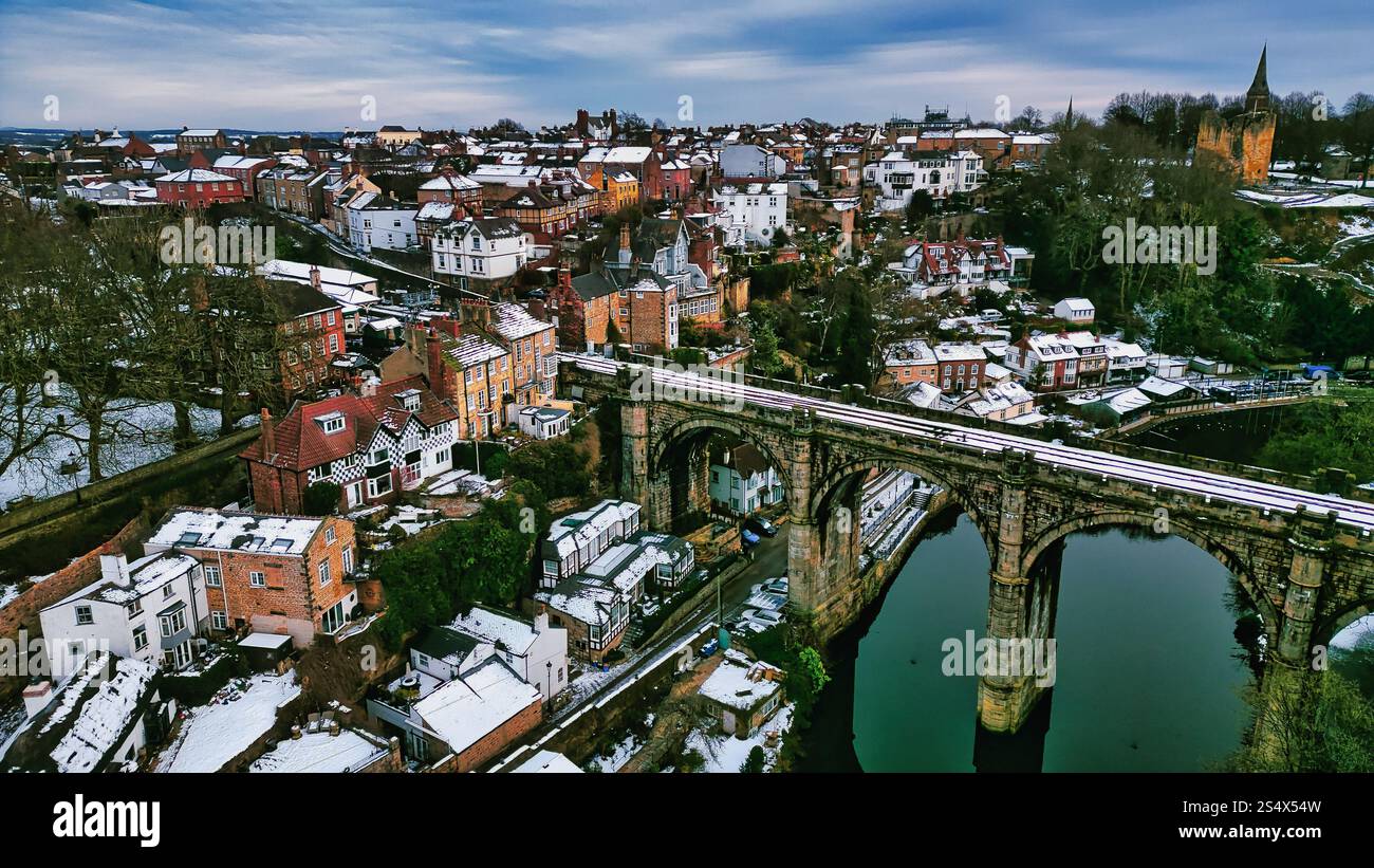Aerial view of a snow-covered town with a stone viaduct spanning a ...