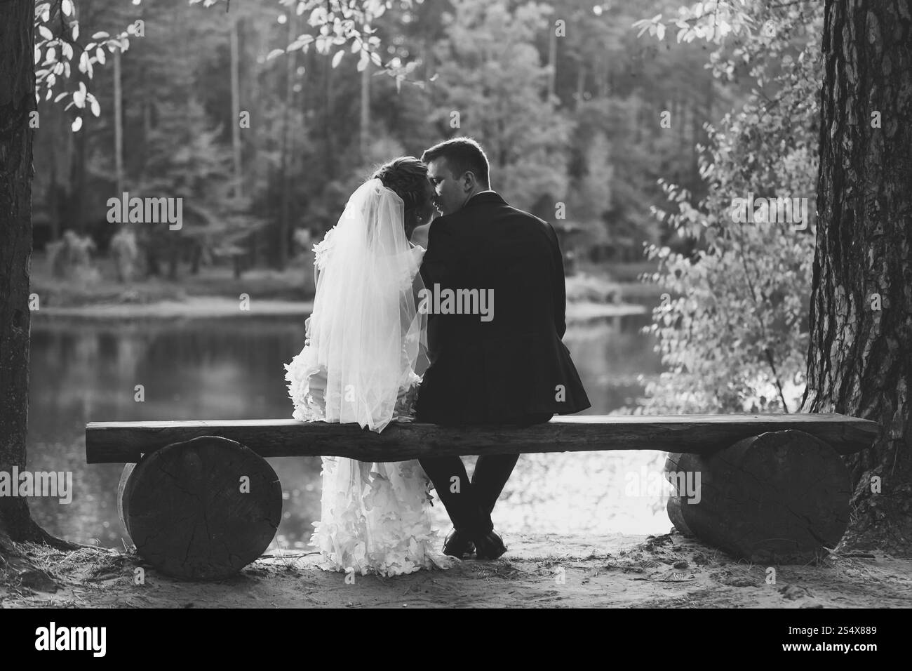 Black and white photo of bride and groom kissing on bench at riverbank ...