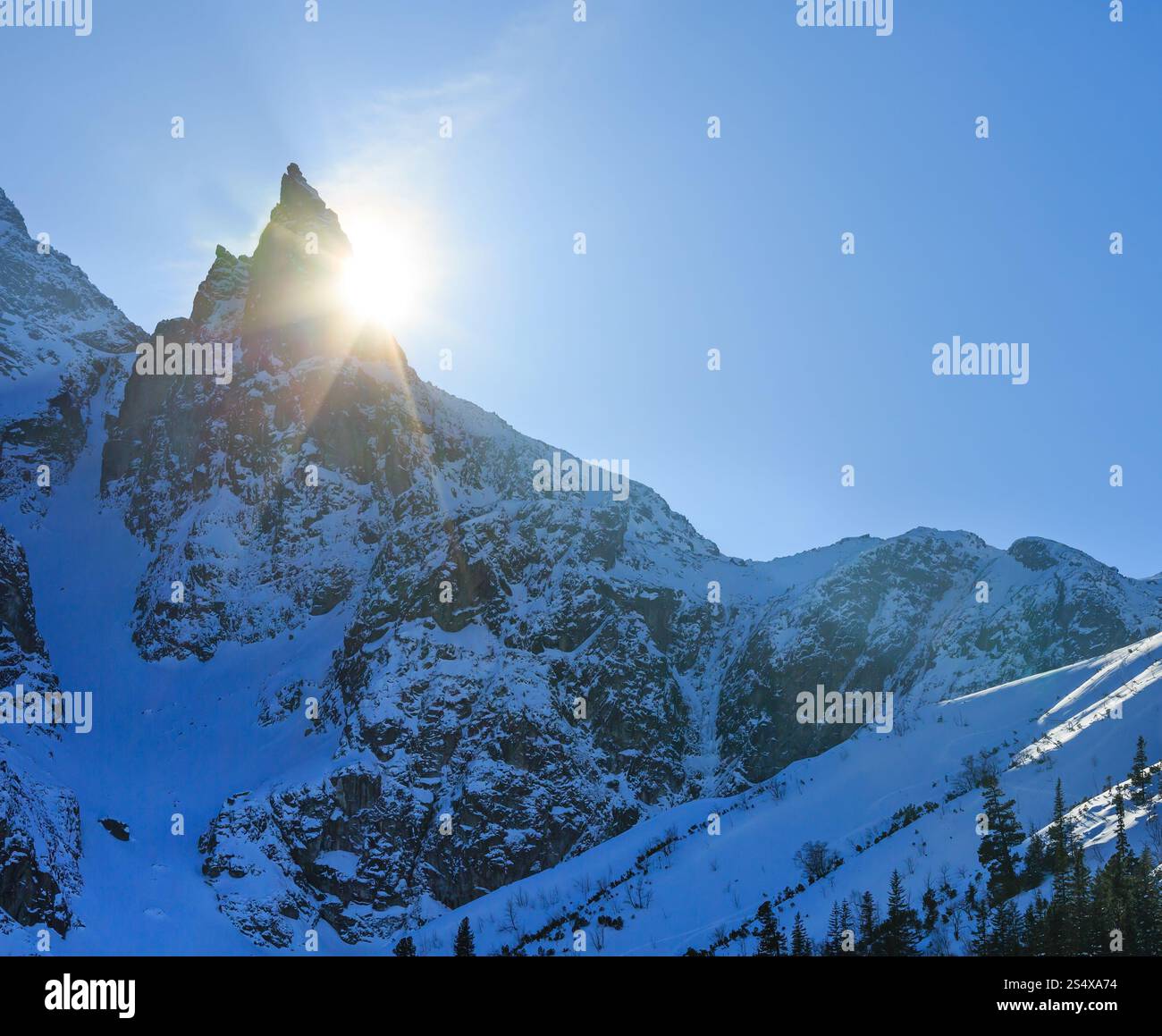Winter rocky mountain view and sun peeks out from behind the rocks ...